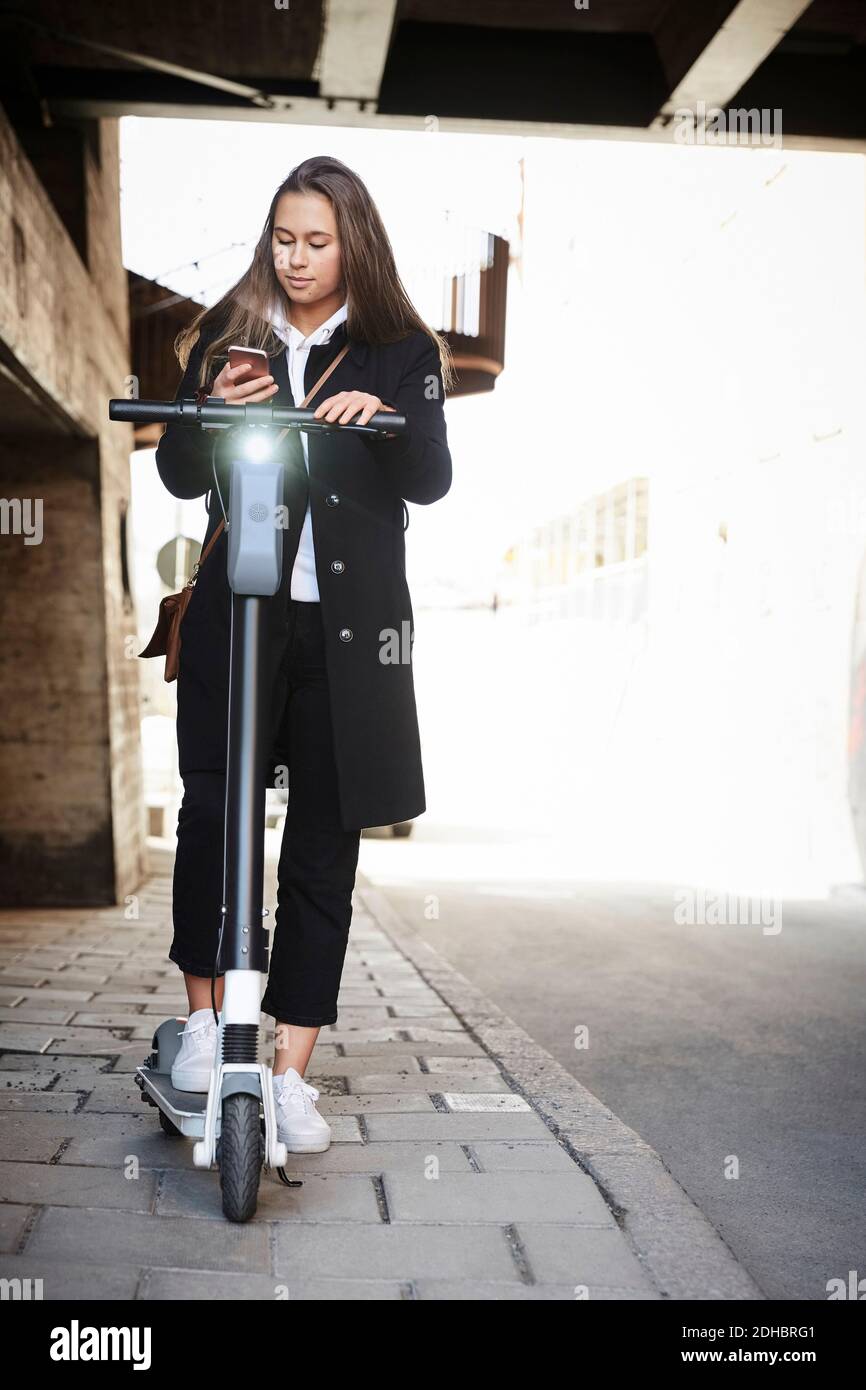 Teenage girl with electric push scooter using mobile phone on footpath ...