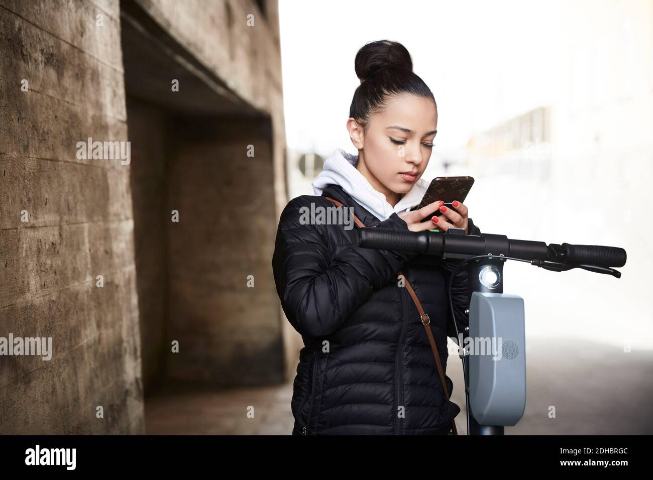 Teenage girl with electric push scooter using mobile phone by wall ...
