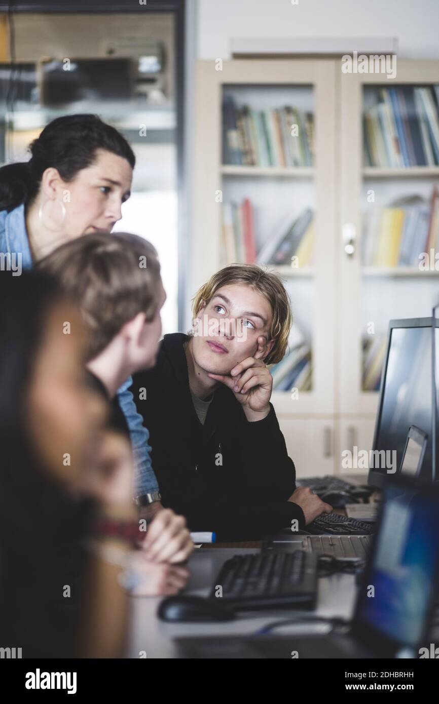Confident female mature teacher discussing with male students while ...