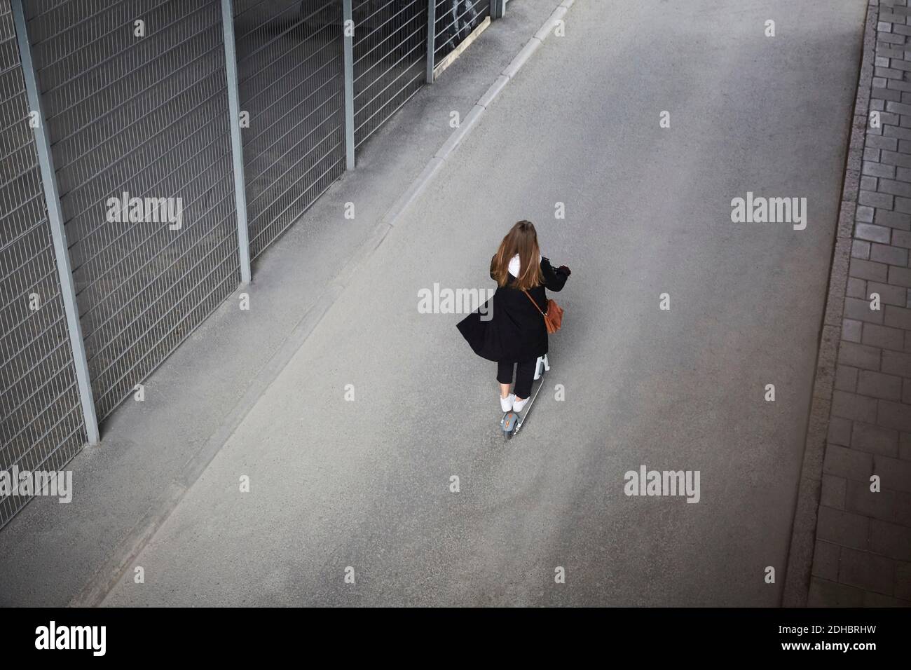 Rear view of teenage girl riding electric push scooter on street in ...