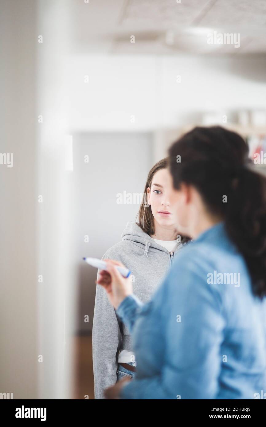 Mature female teacher explaining to teenage girl while standing in ...