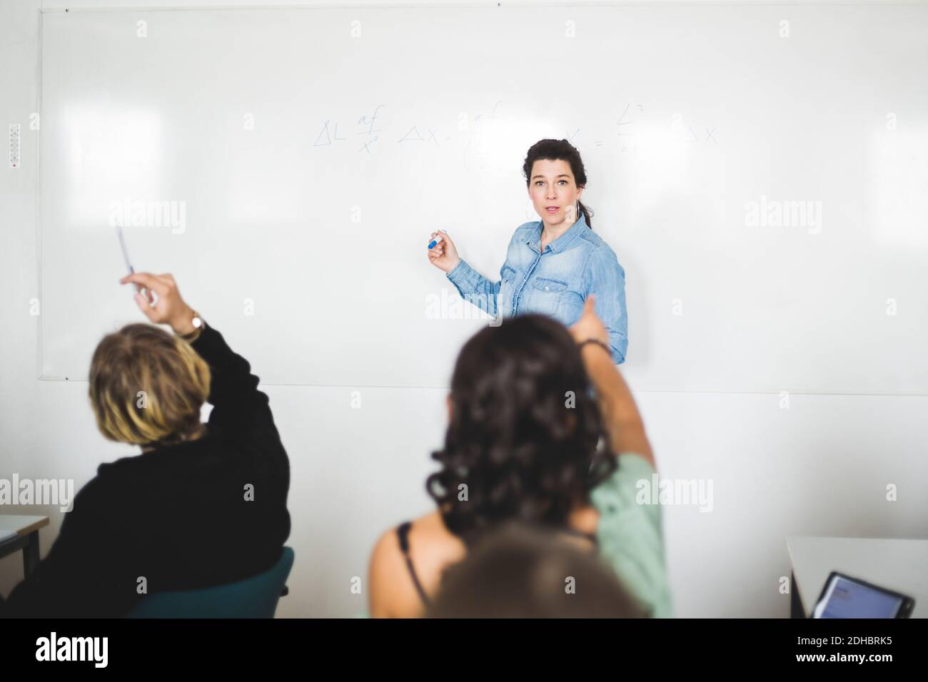 Students pointing at teacher standing against whiteboard in classroom ...