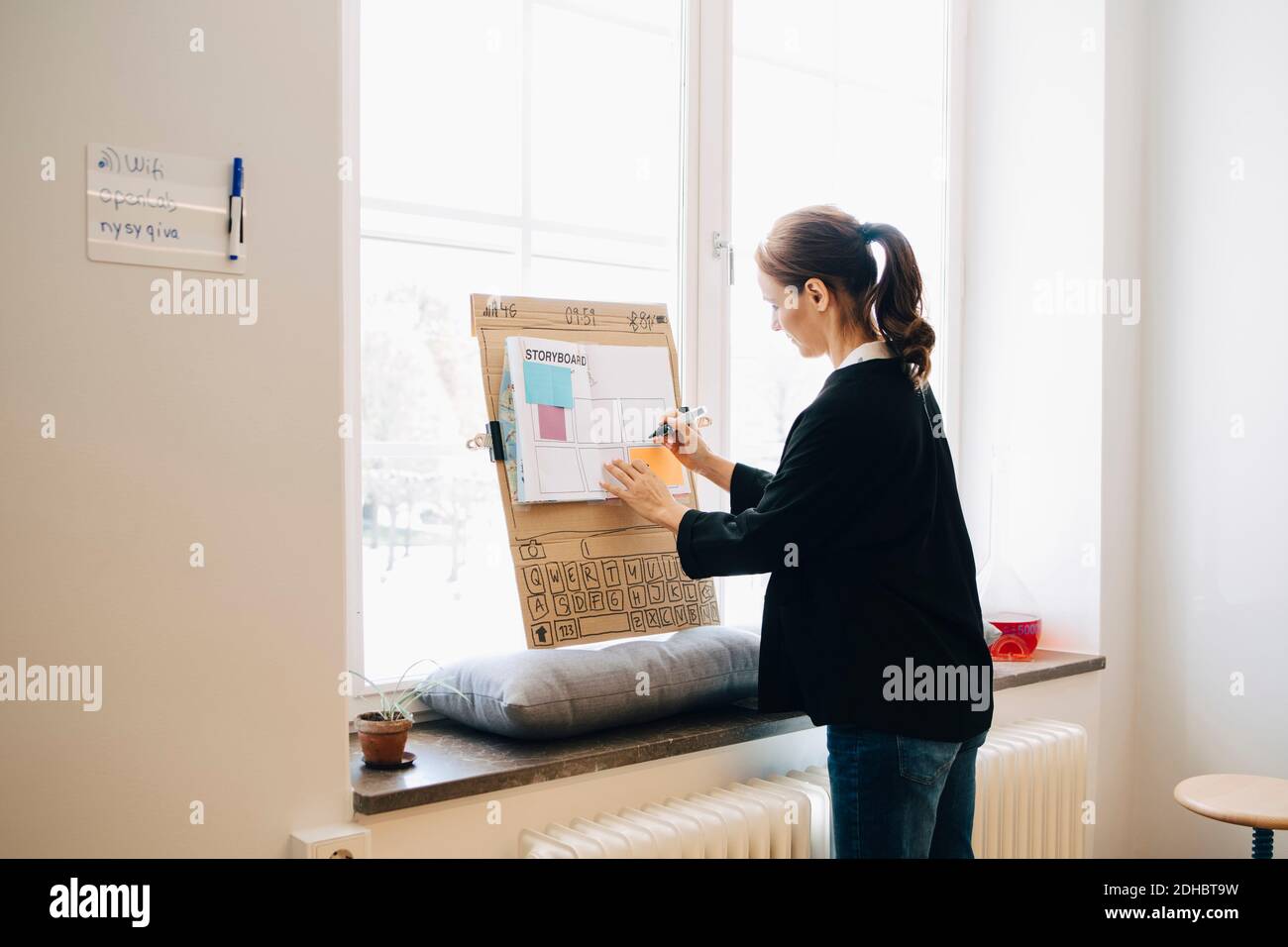 Confident businesswoman writing strategy on placard over window sill at ...
