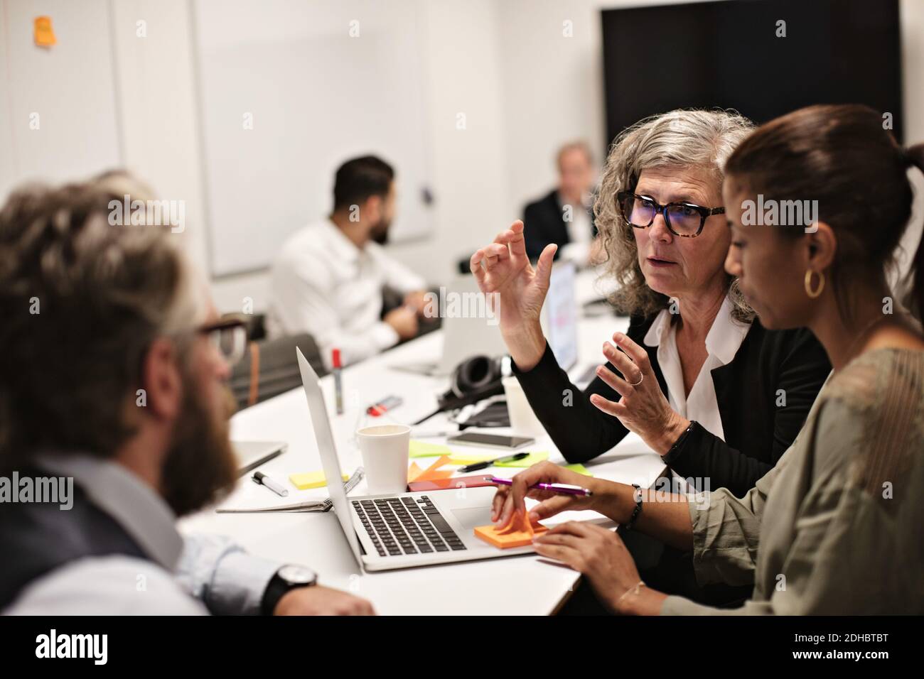 Confident mature professional discussing with colleagues in meeting at ...