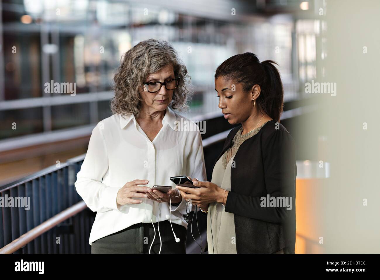 Female business colleagues talking while using smart phones at office ...