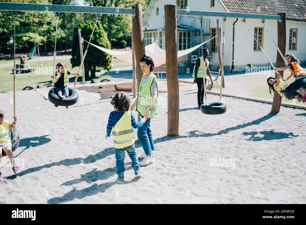 Teachers standing while students enjoying on swing in playground Stock ...