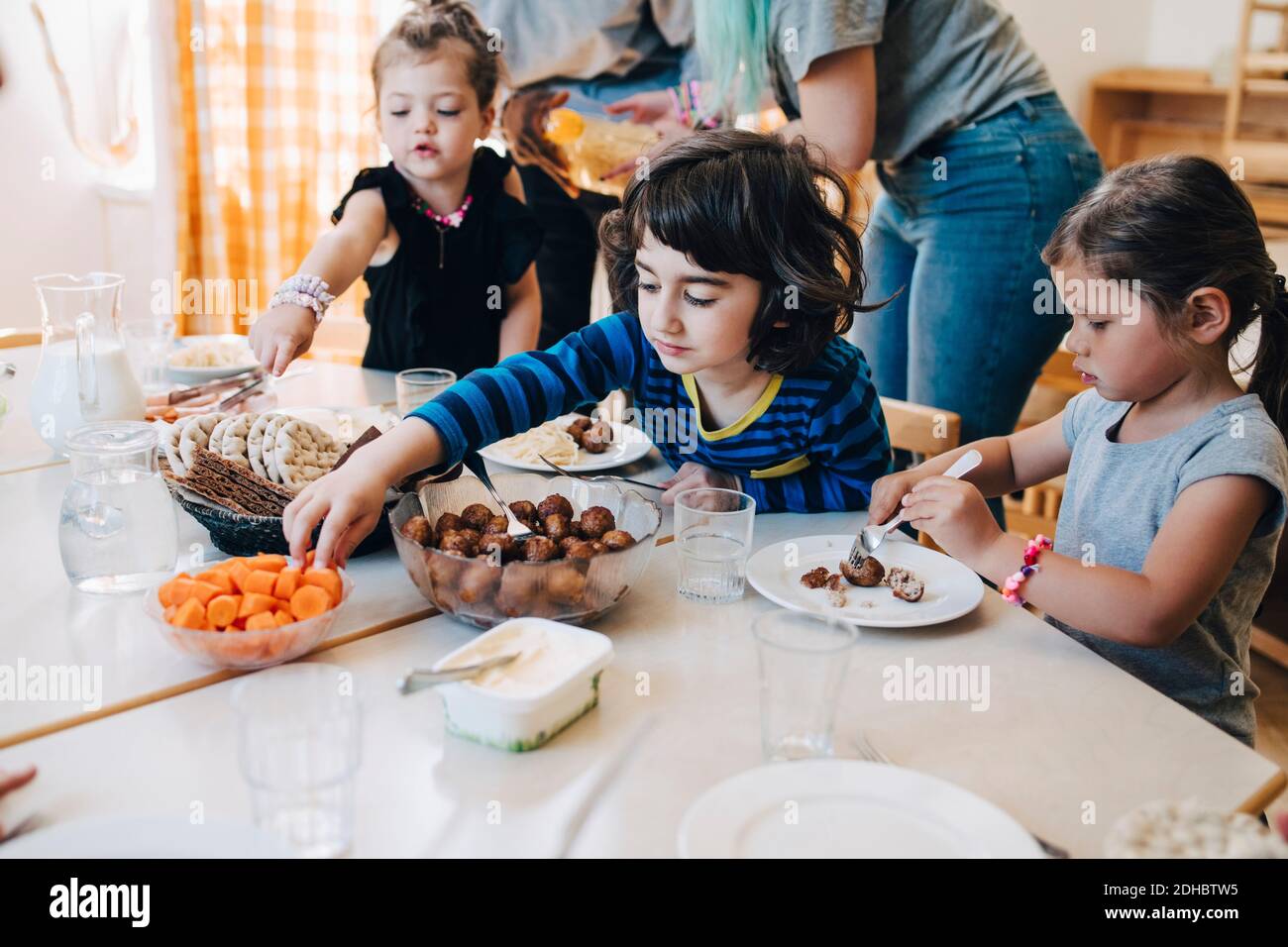 Students eating lunch at table against teachers standing in classroom ...