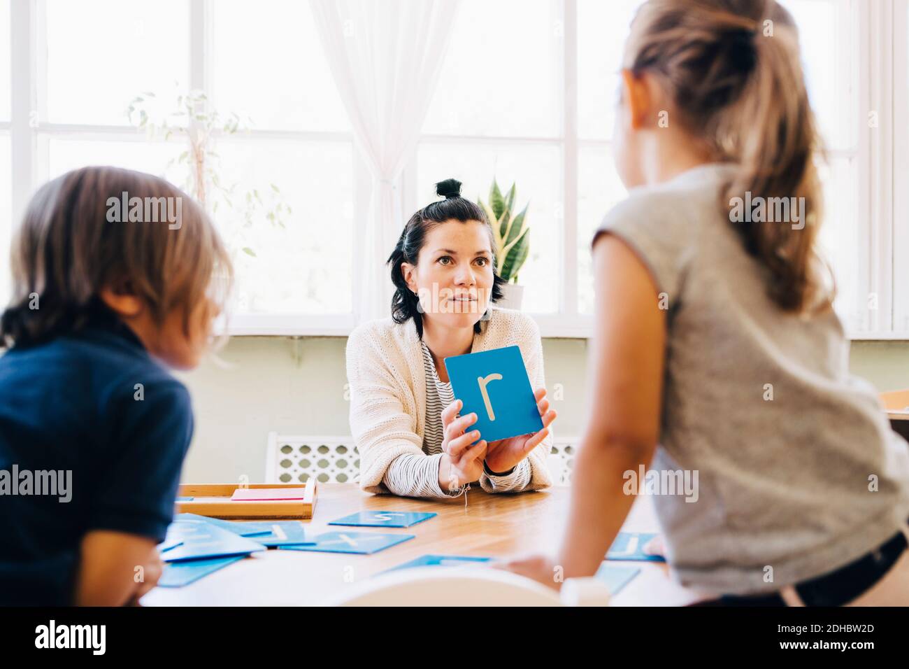 Confident female teacher showing letter R to students at table in ...
