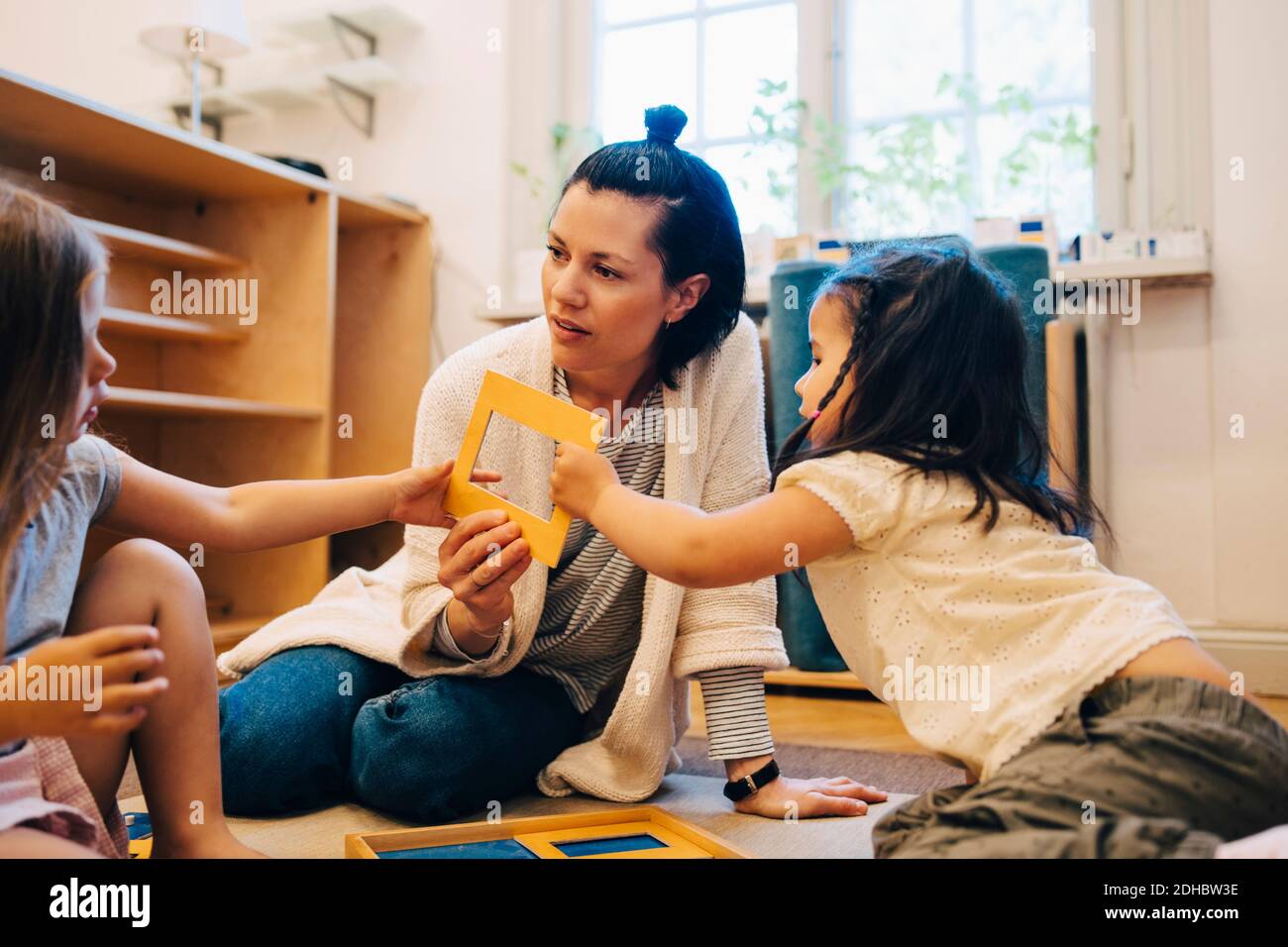 Female teacher and students holding picture frame while sitting in ...