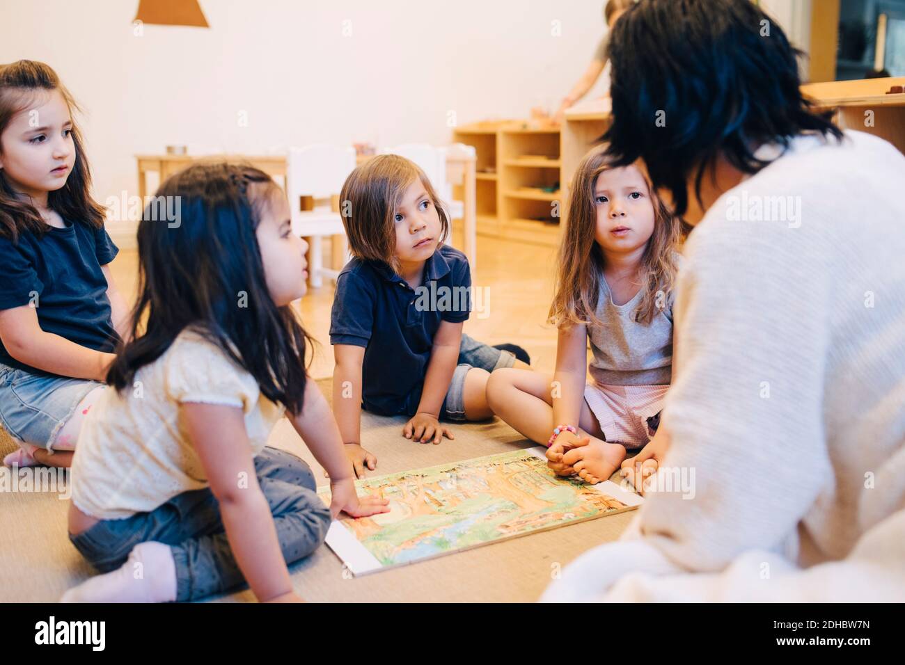 Female teacher telling story to students sitting in classroom at child ...