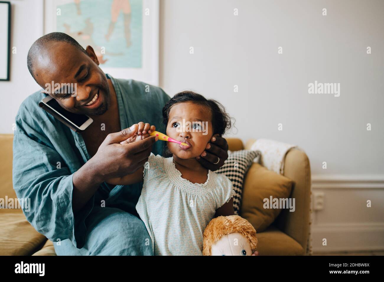 Man talking on mobile phone while brushing daughter's teeth at home ...