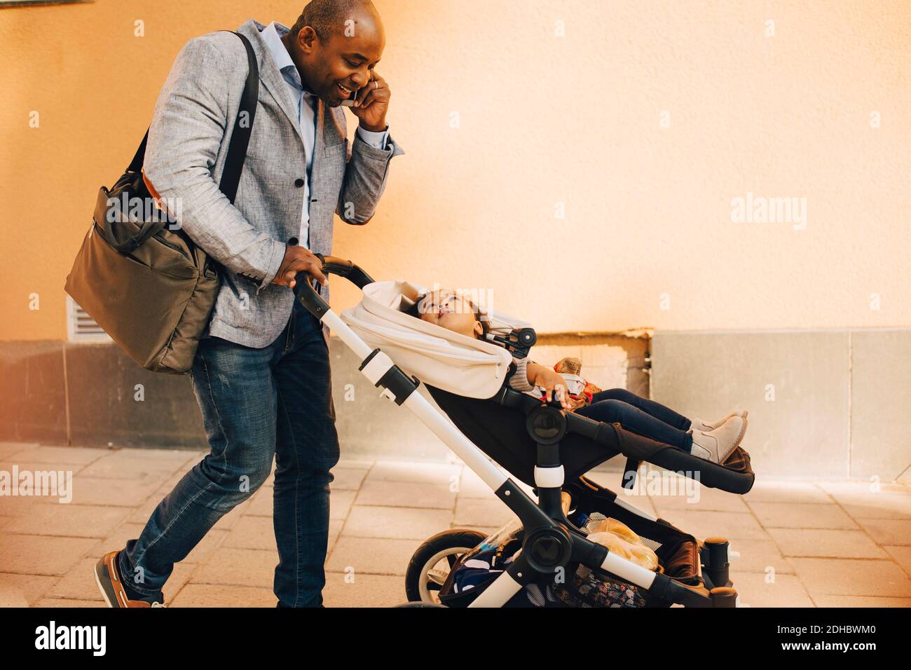 Smiling father talking on mobile phone while pushing daughter in ...