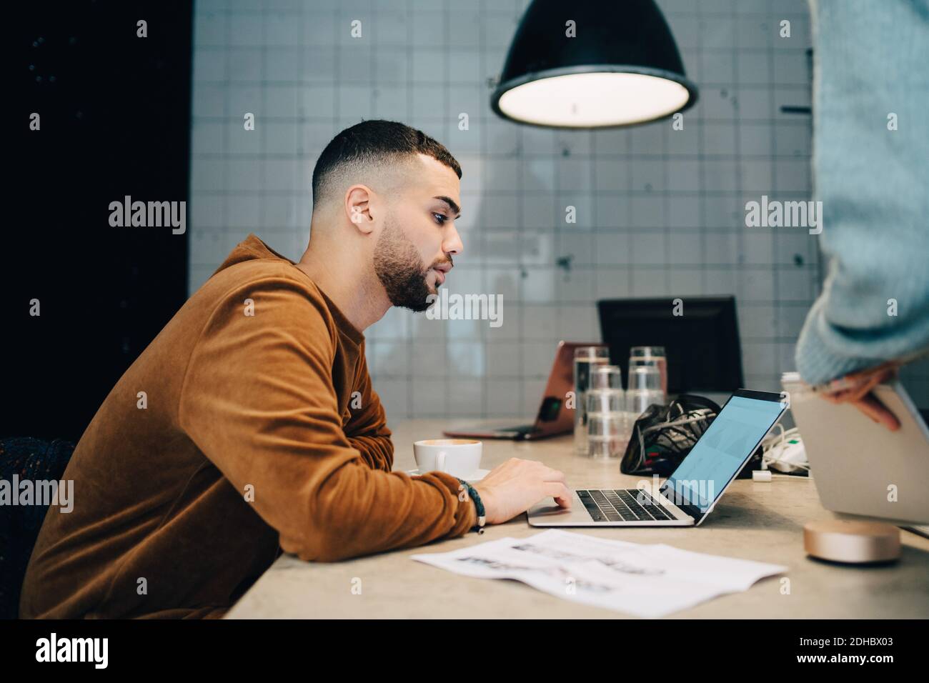 Side view of young male hacker using laptop at desk in small office ...