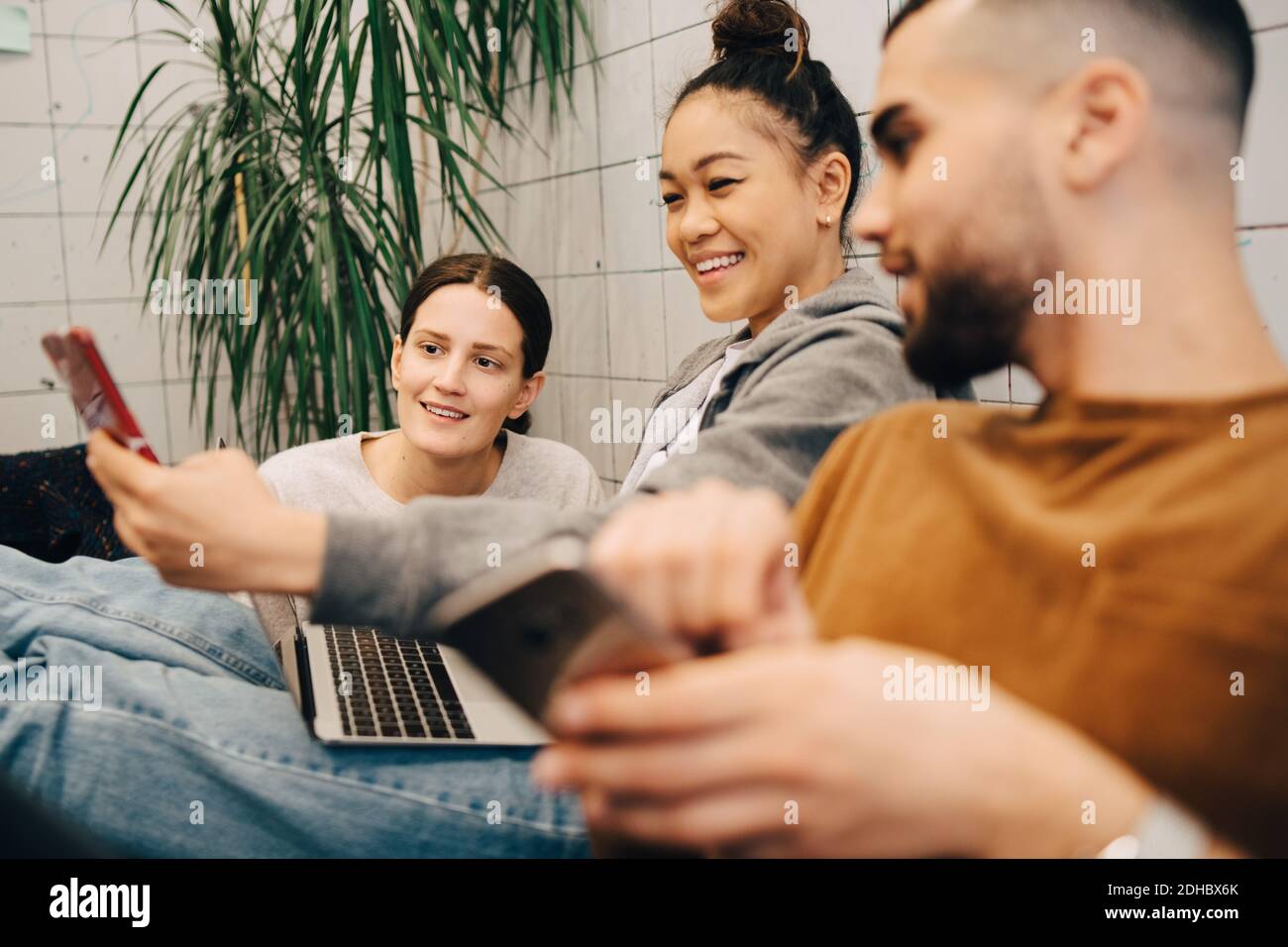 Smiling young businesswoman sharing mobile phone with colleagues while ...