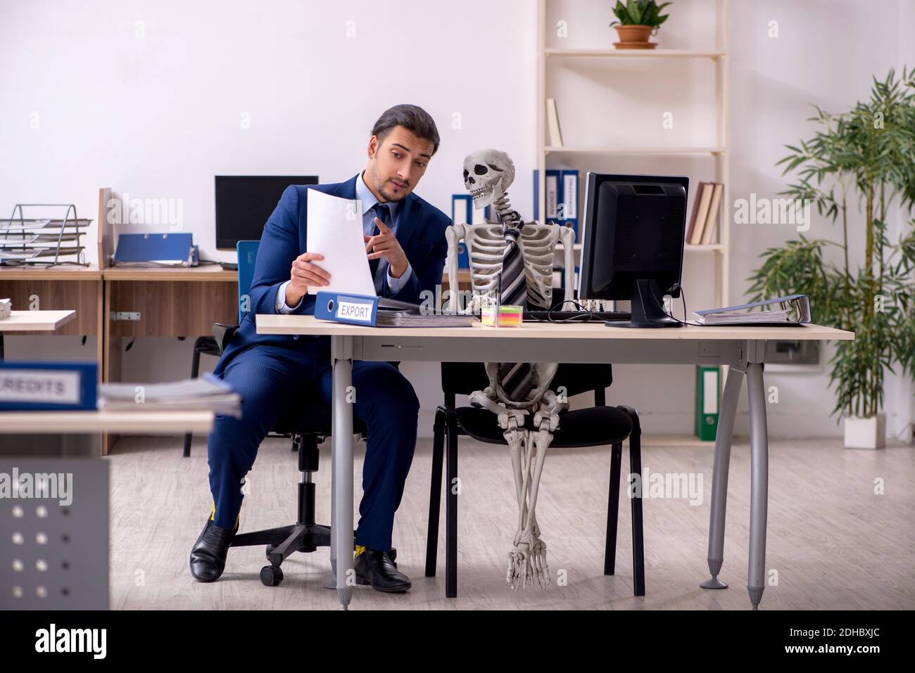 Young male employee with skeletons in the office Stock Photo - Alamy
