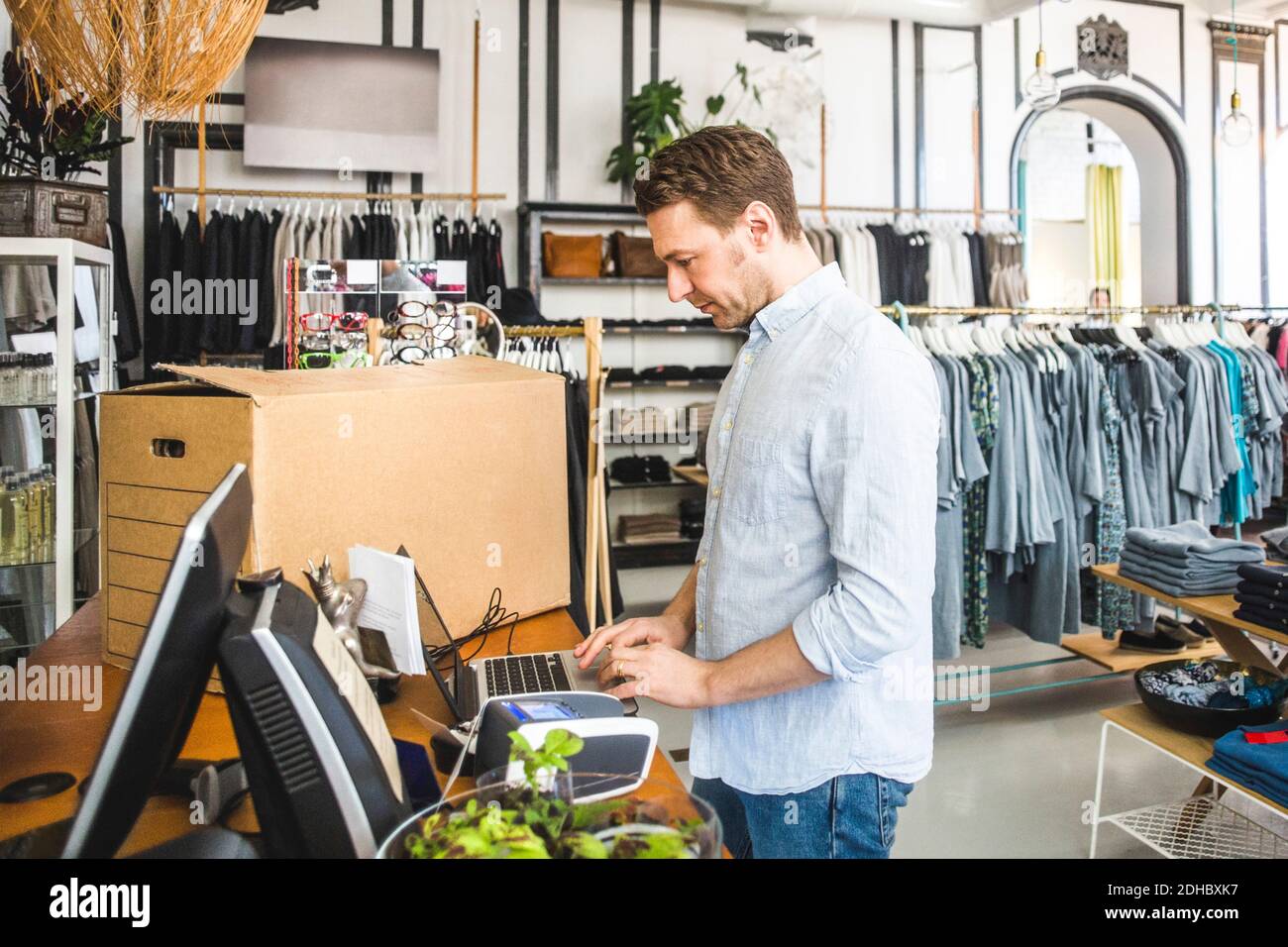 Side view of salesman using laptop while standing in clothing store ...
