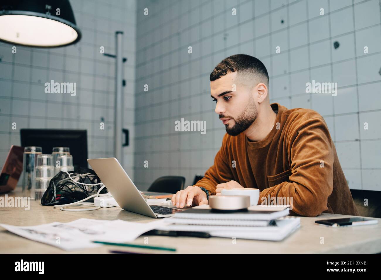 Confident young male computer programmer using laptop at desk in small ...