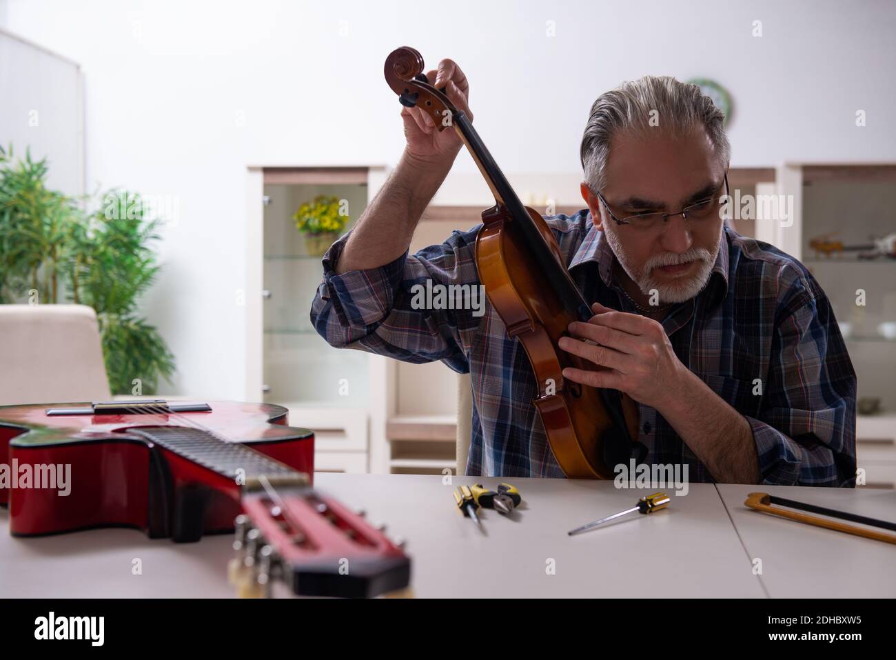 Senior male repairman repairing musical instruments at home Stock Photo ...