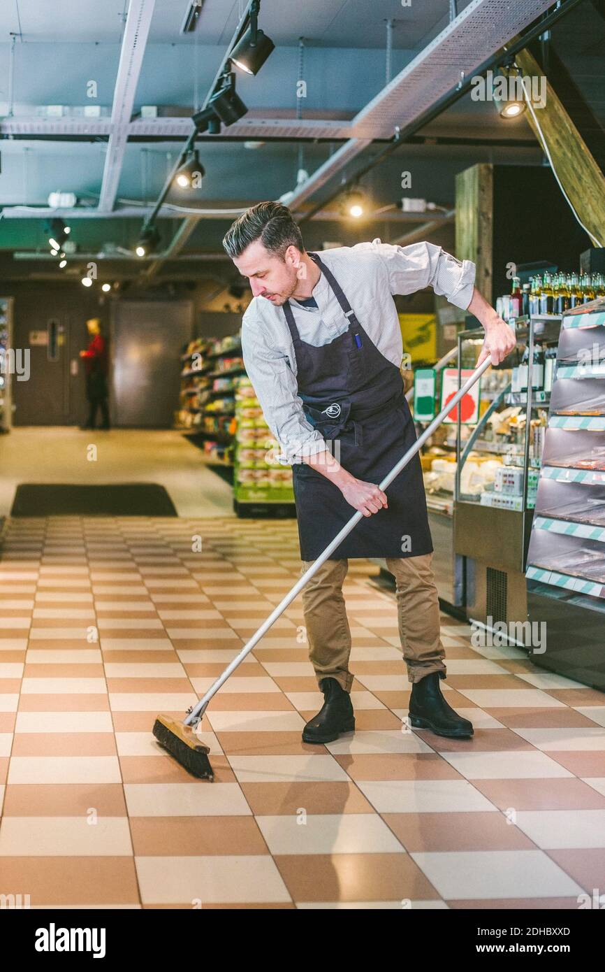 Full length of salesman sweeping floor in grocery store Stock Photo - Alamy