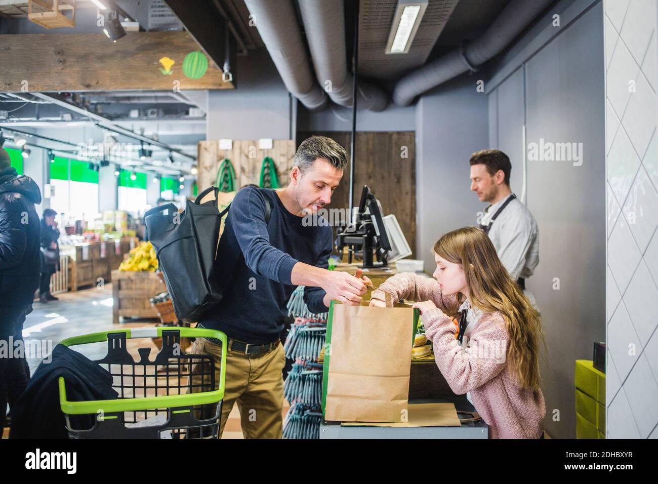 Father and daughter packing groceries in paper bag at checkout counter ...