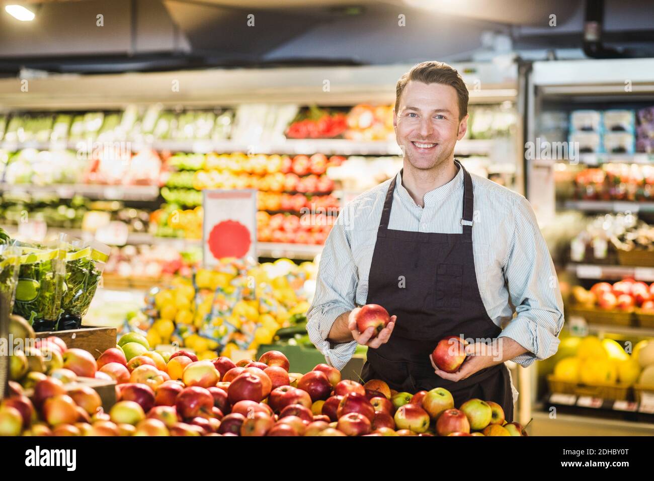 Portrait of smiling mature owner standing at apple stall in grocery ...