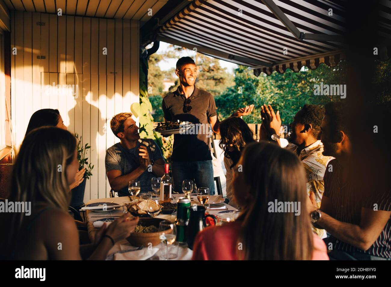 Friends at dining table clapping for man serving food in dinner party ...