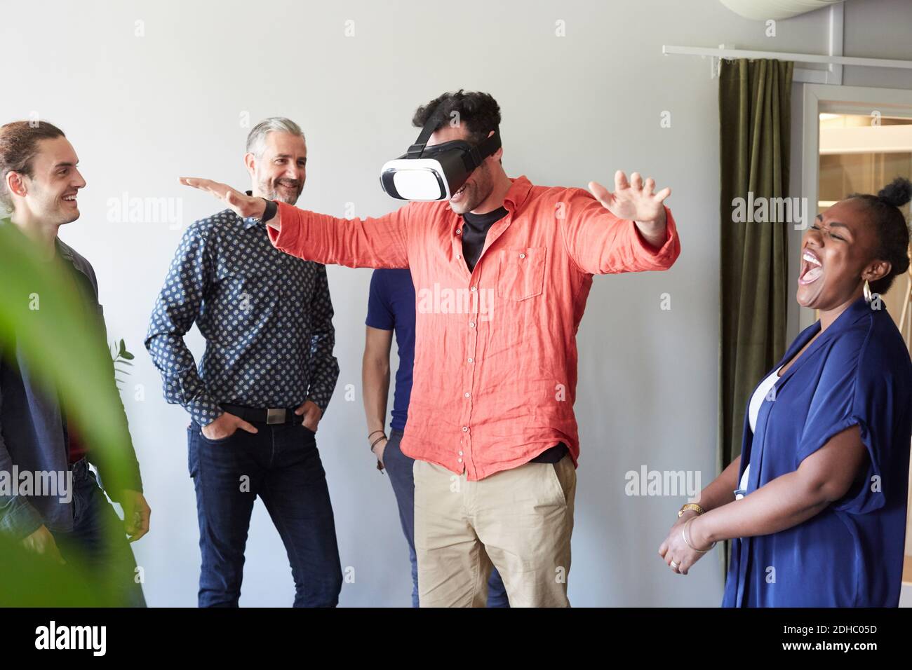 Happy business people looking at male colleague using virtual reality ...