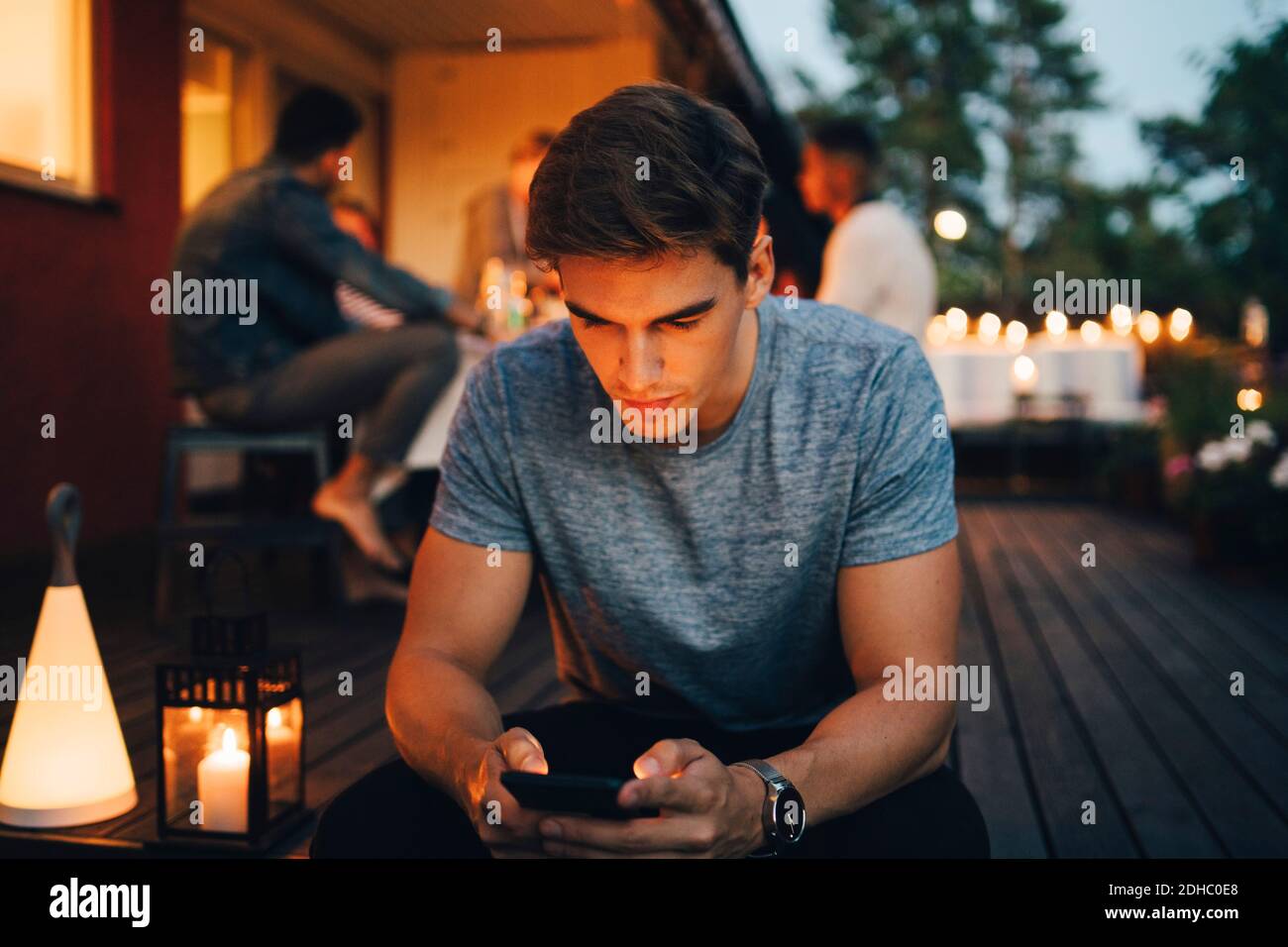 Young man using smart phone while friends in background during dinner ...