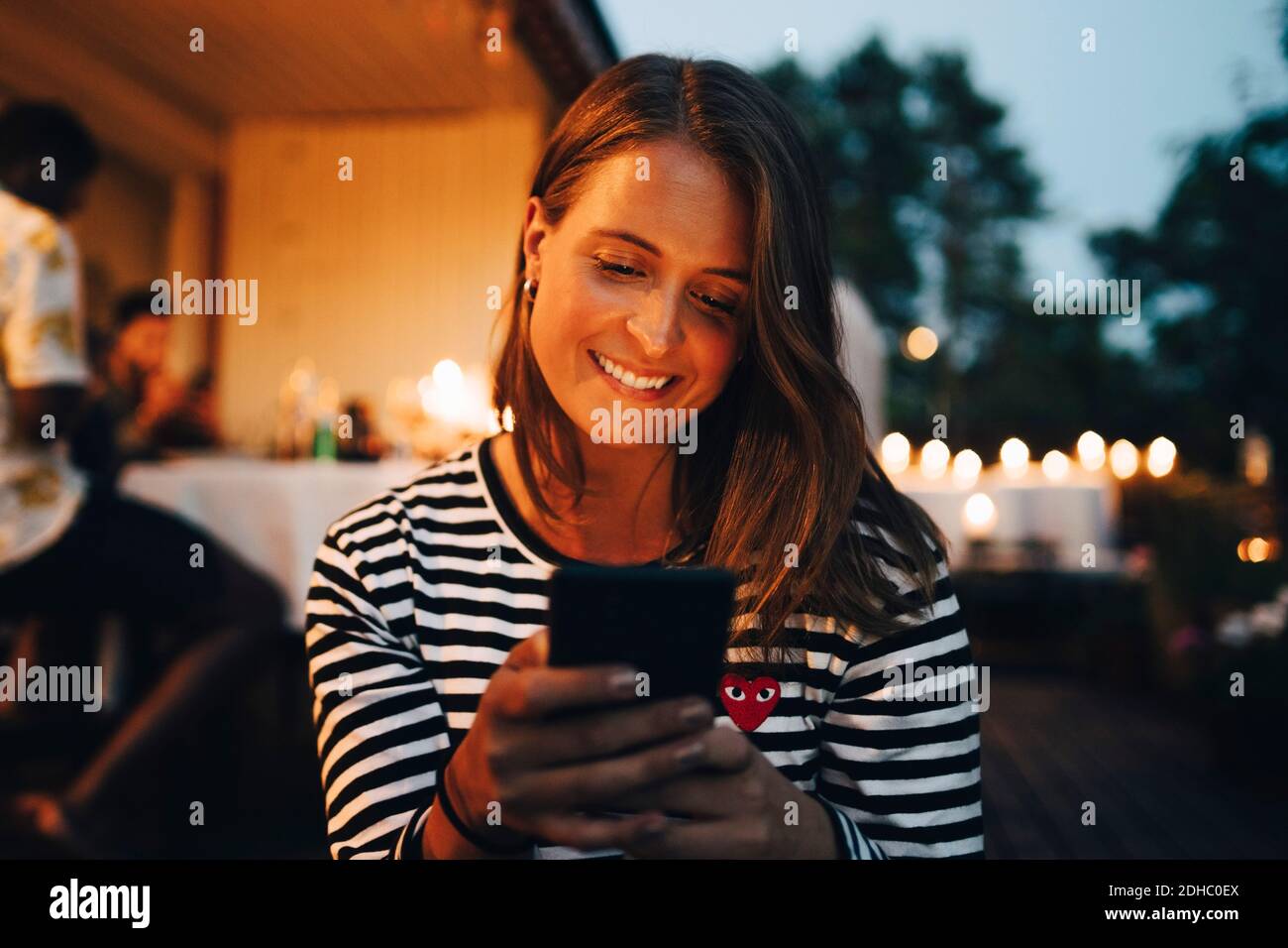 Smiling young woman using smart phone while friends in background ...