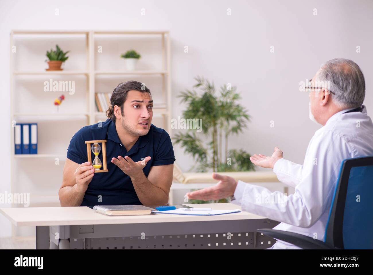 Young male patient visiting old doctor in time management concep Stock ...