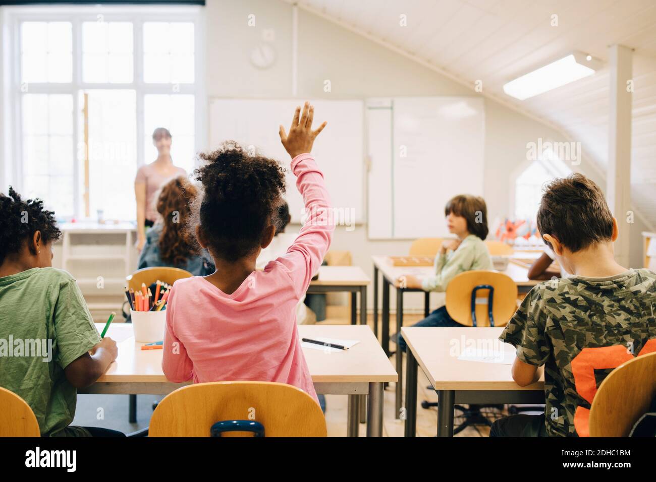 Rear view of boy raising hand while answering in class at elementary ...