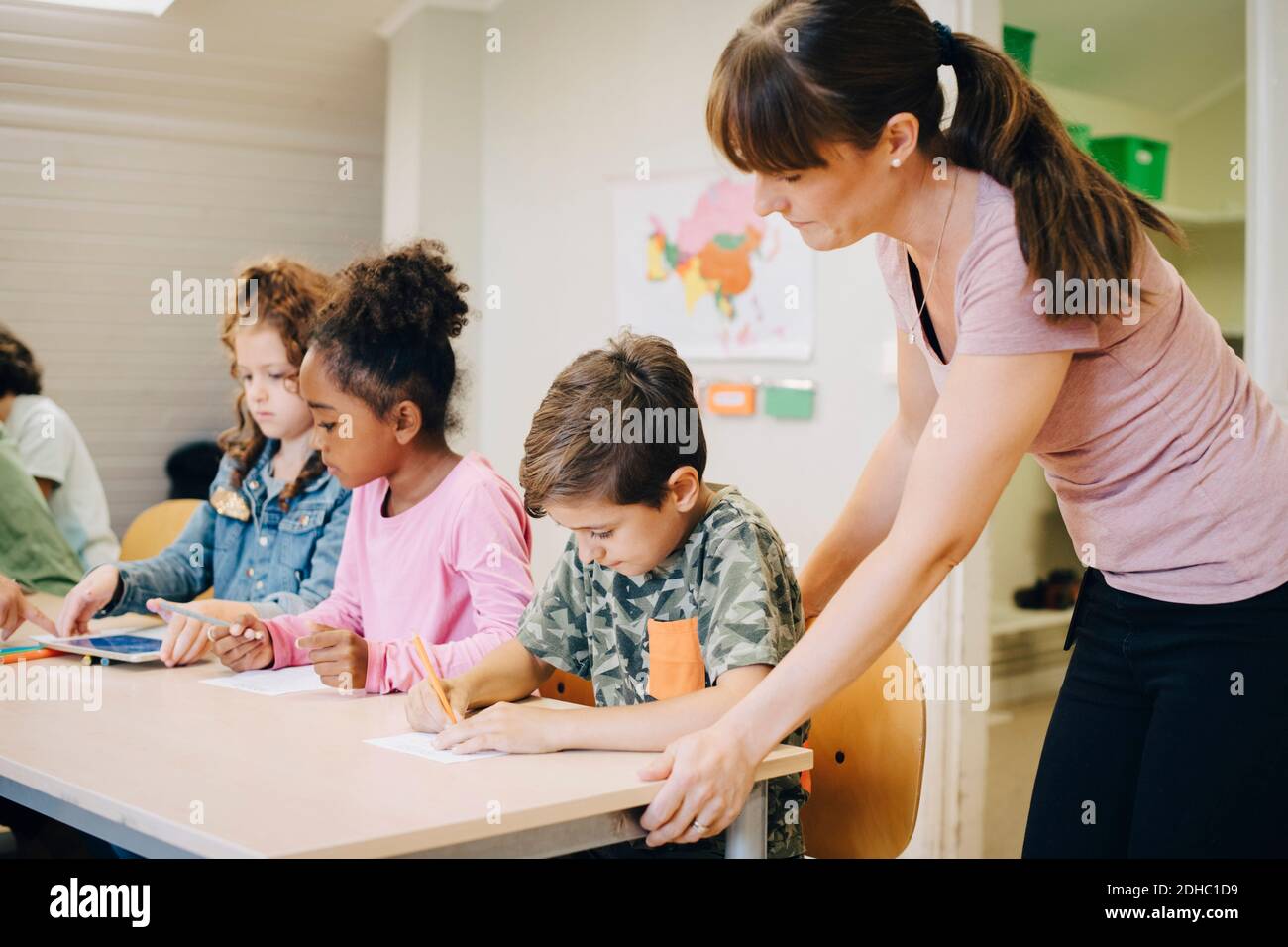 Female teacher assisting students in learning at classroom Stock Photo ...