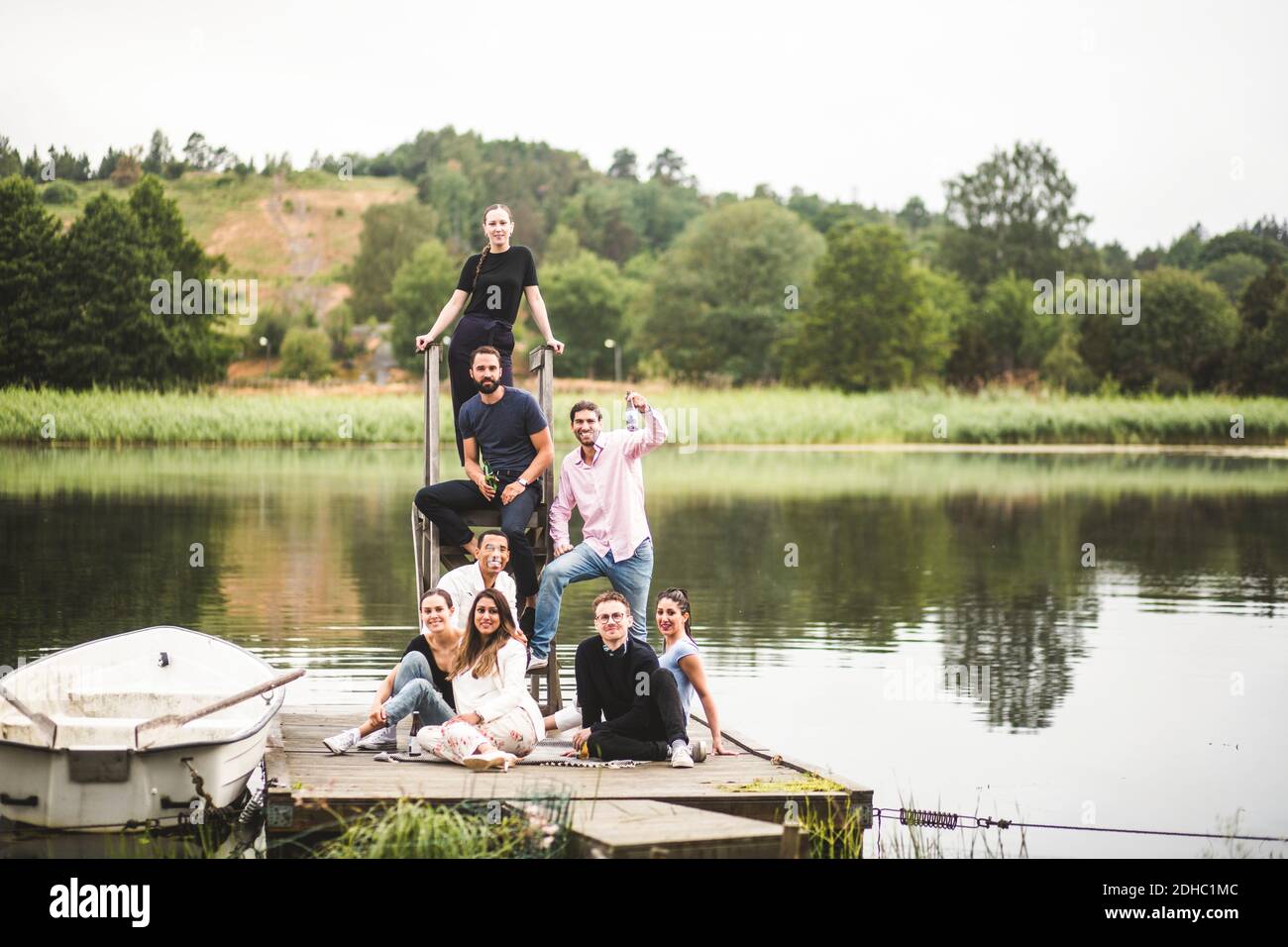 Portrait of happy male and female friends on jetty over lake during ...