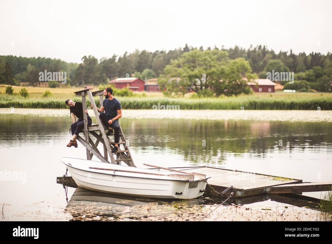 Boyfriend and girlfriend sitting on diving platform at jetty by lake ...