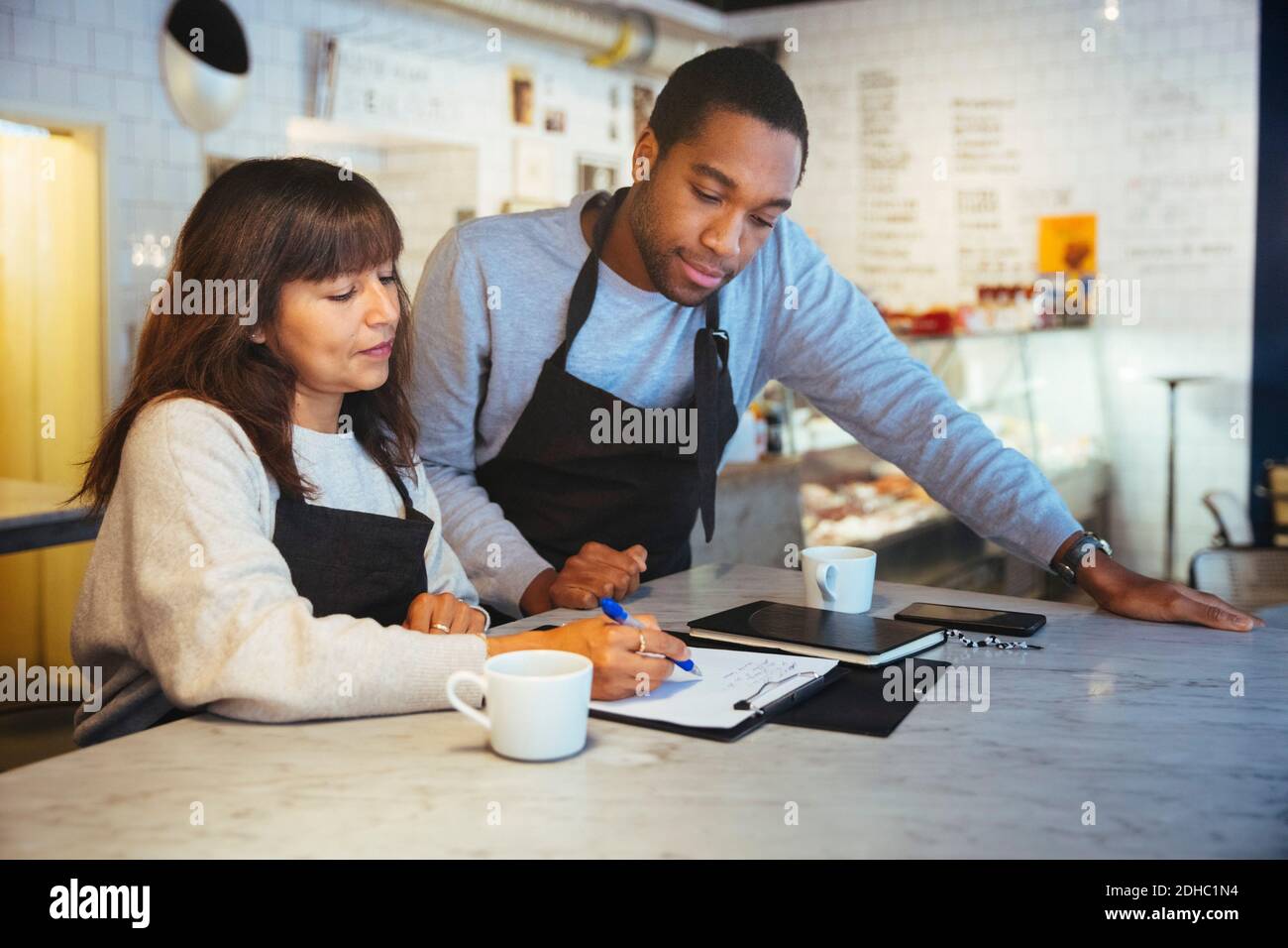 Female employee discussing over clipboard with male coworker at table ...