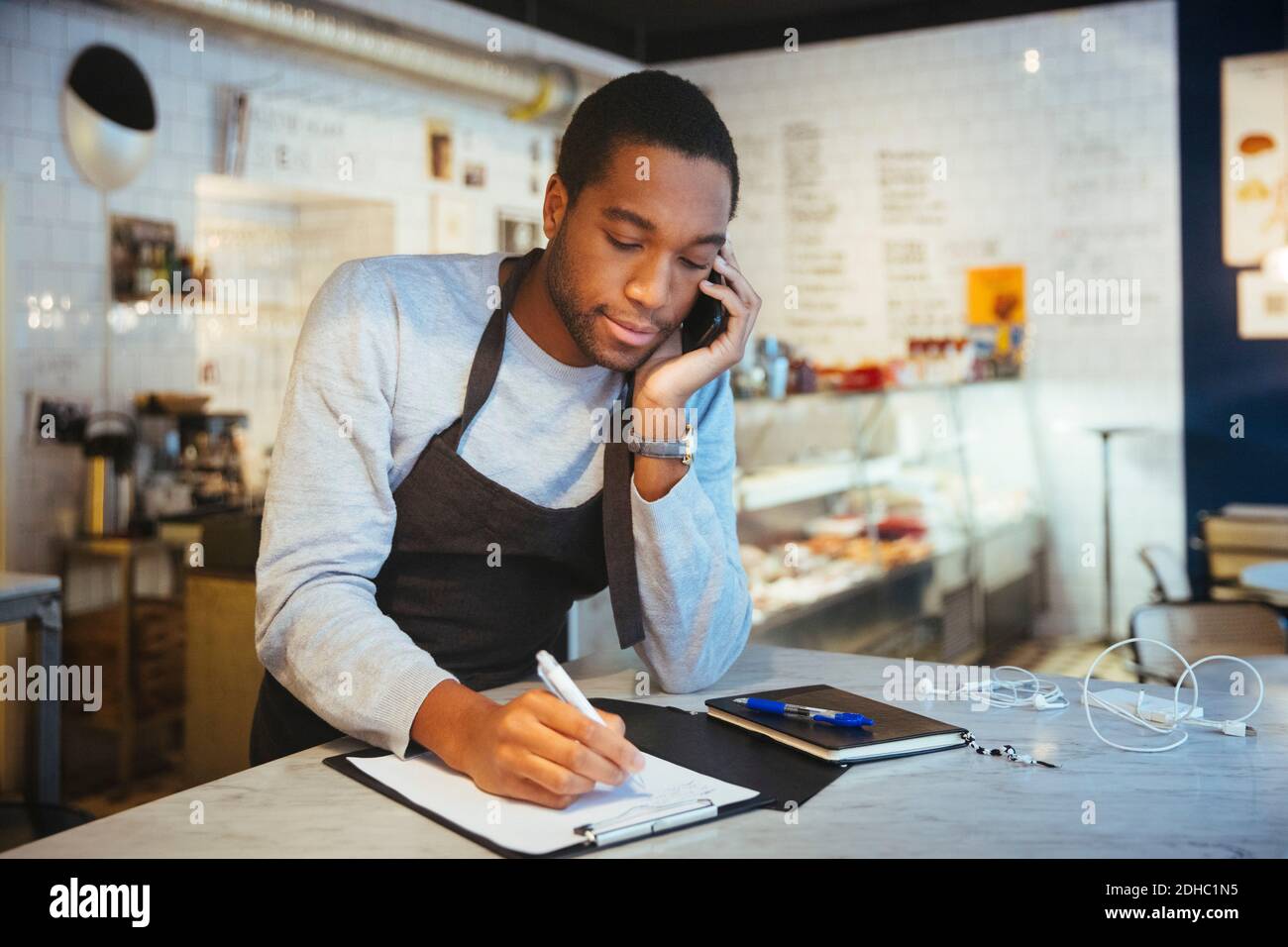 Confident young male employee talking through smart phone while writing ...
