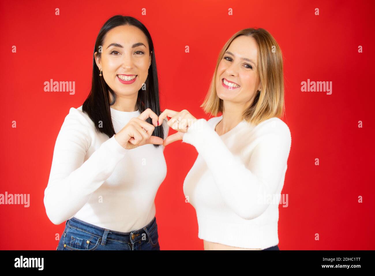 Happy young female friends making heart shape with hands and fingers ...