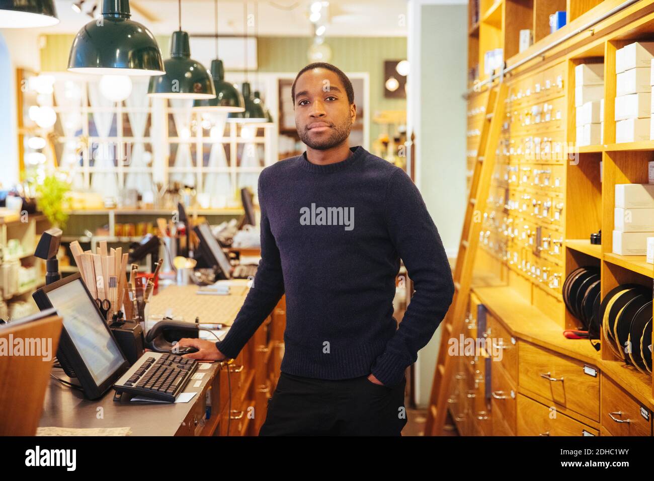 Portrait of confident young male owner standing at checkout counter in ...