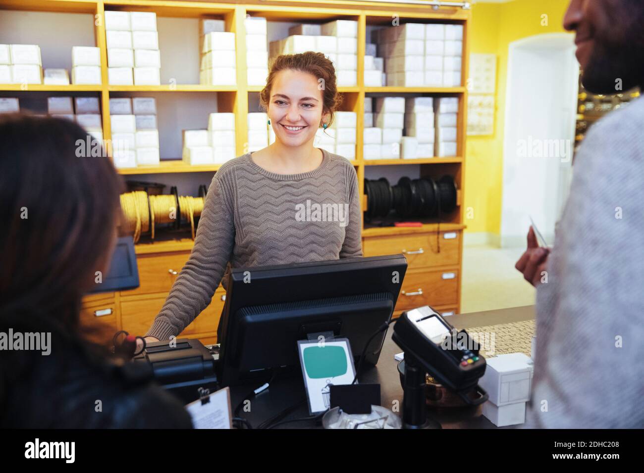 Smiling young female cashier looking at customer standing in furniture ...