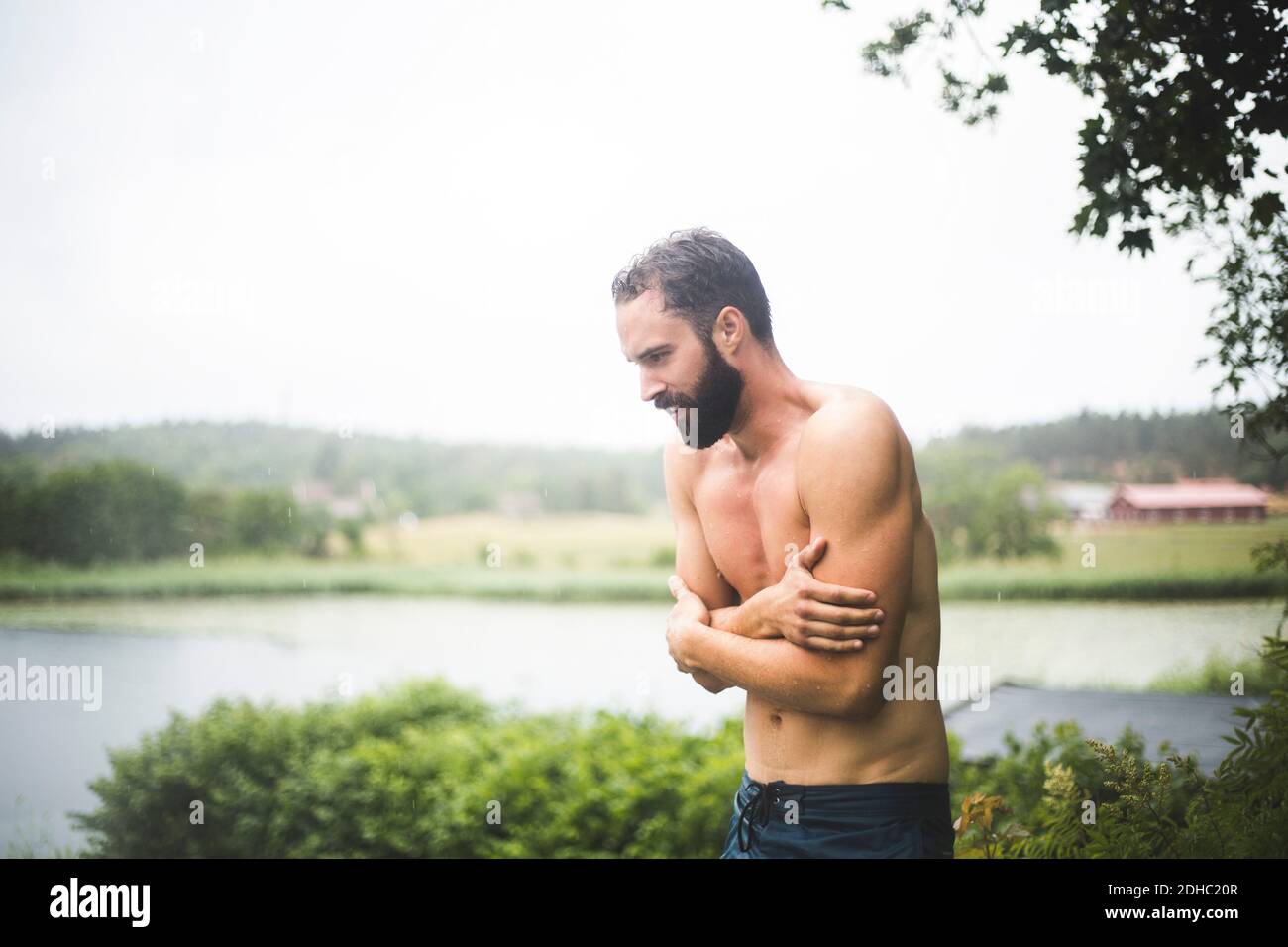 Shirtless mid adult man shivering while standing in backyard during ...