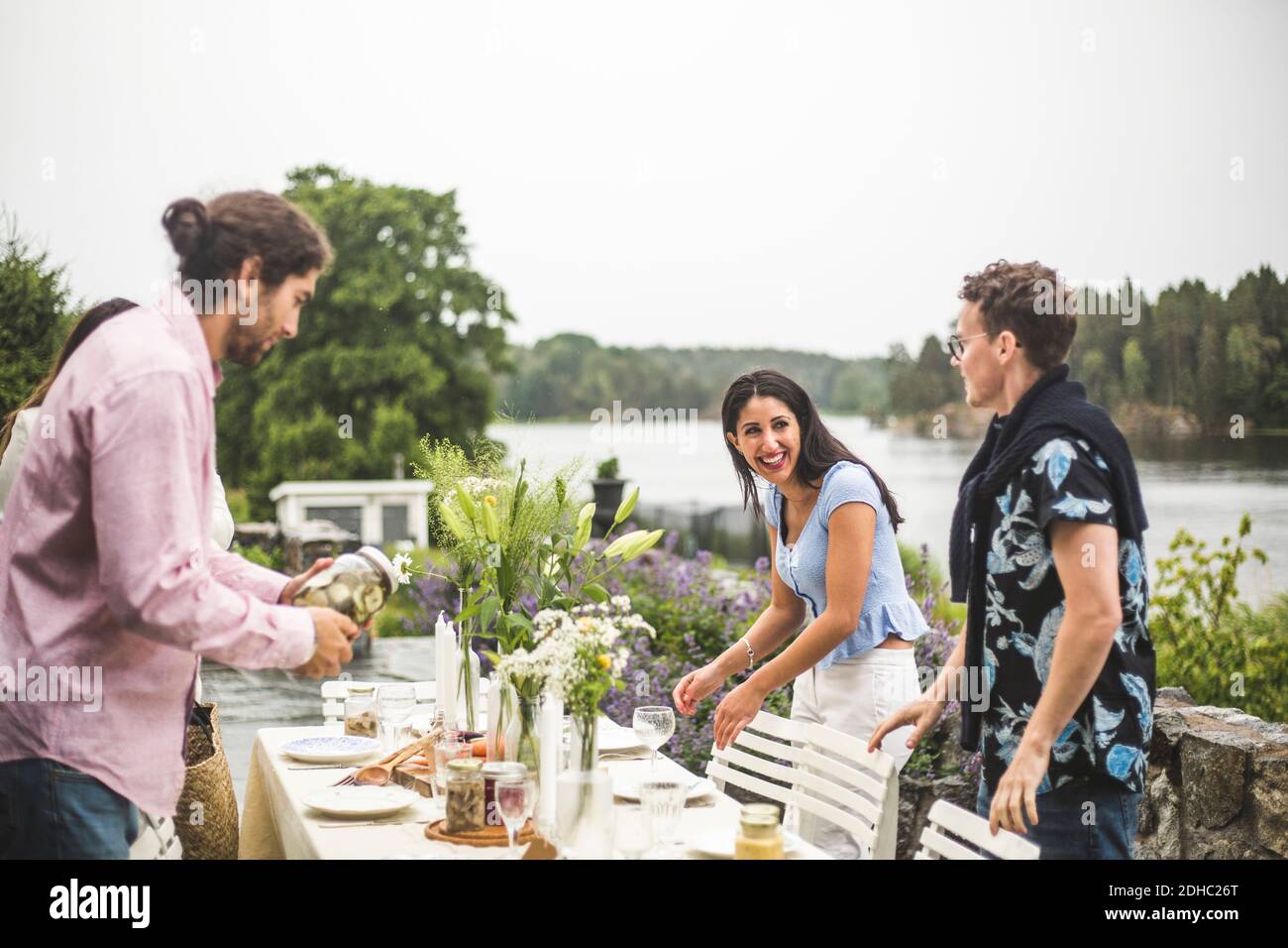 Happy multi-ethnic friends setting table for dinner party in backyard ...