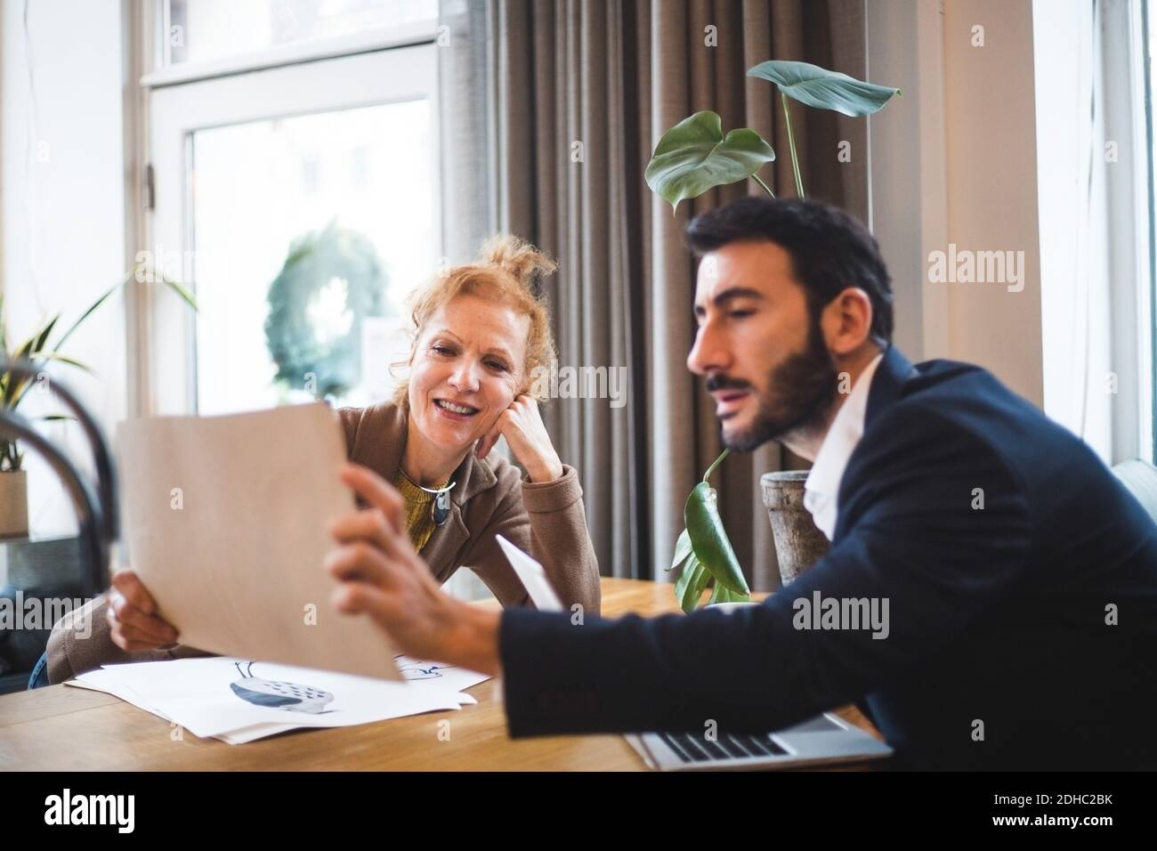 Smiling female illustrator showing drawing to male professional at ...