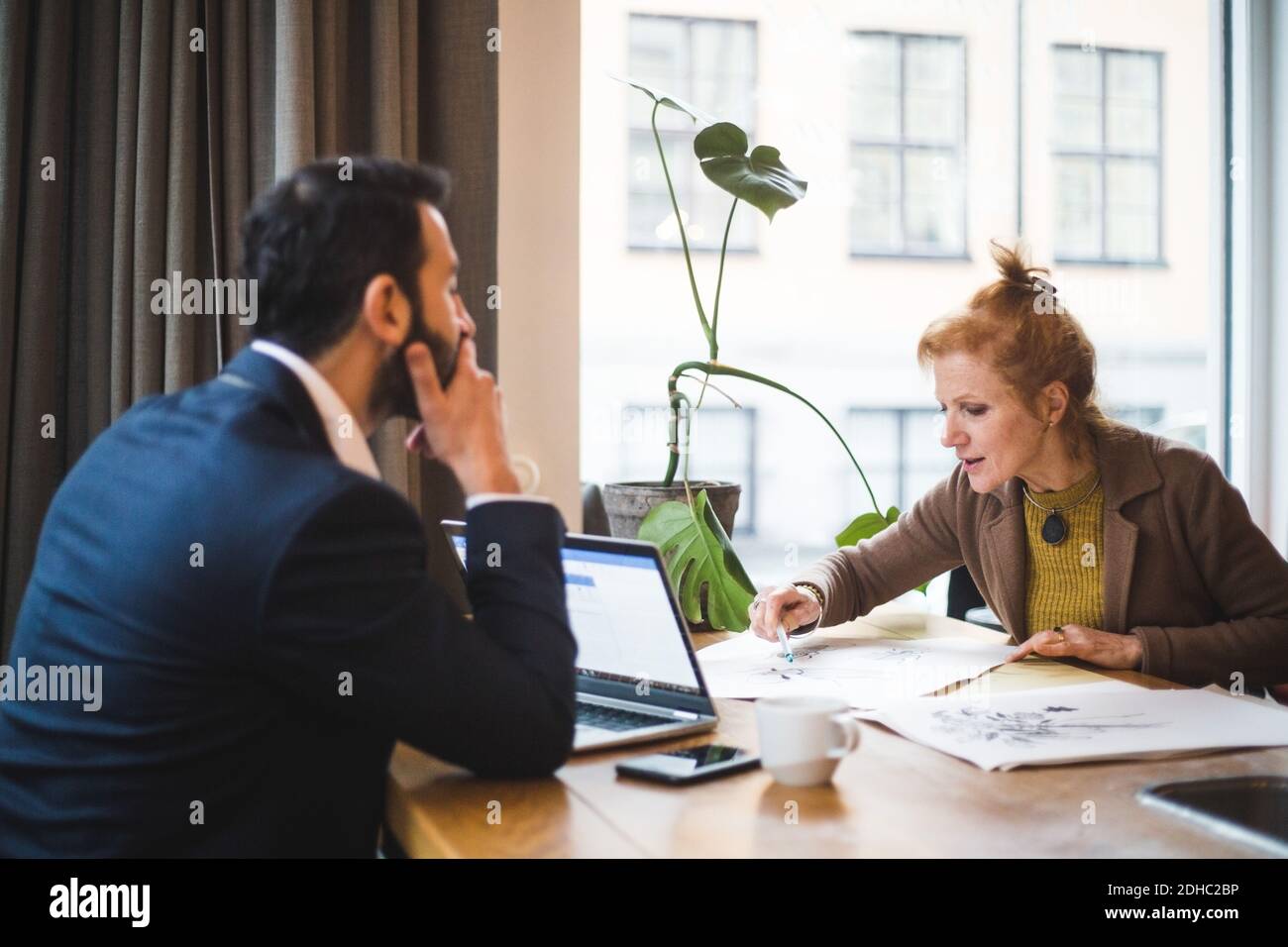Confident female illustrator discussing over drawing with male ...