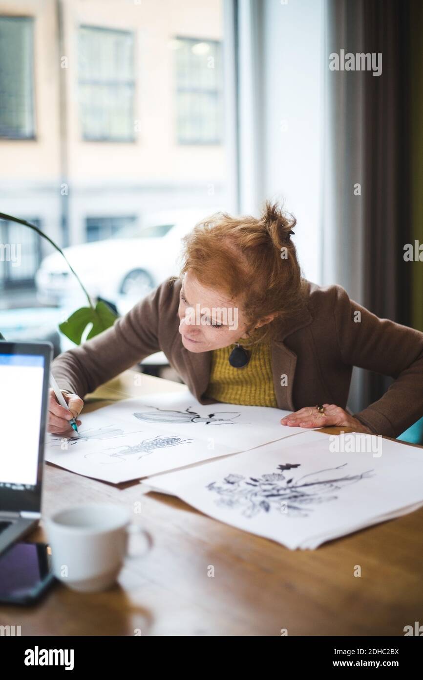 Confident female illustrator drawing on paper at table in office Stock ...