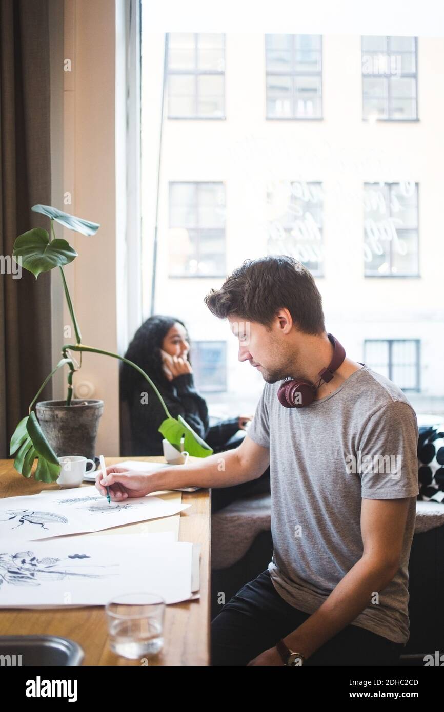 Confident male illustrator drawing on paper at table in office Stock ...