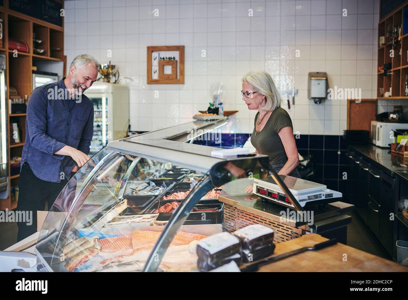 Customer smiling while showing seafood at retail display to saleswoman ...