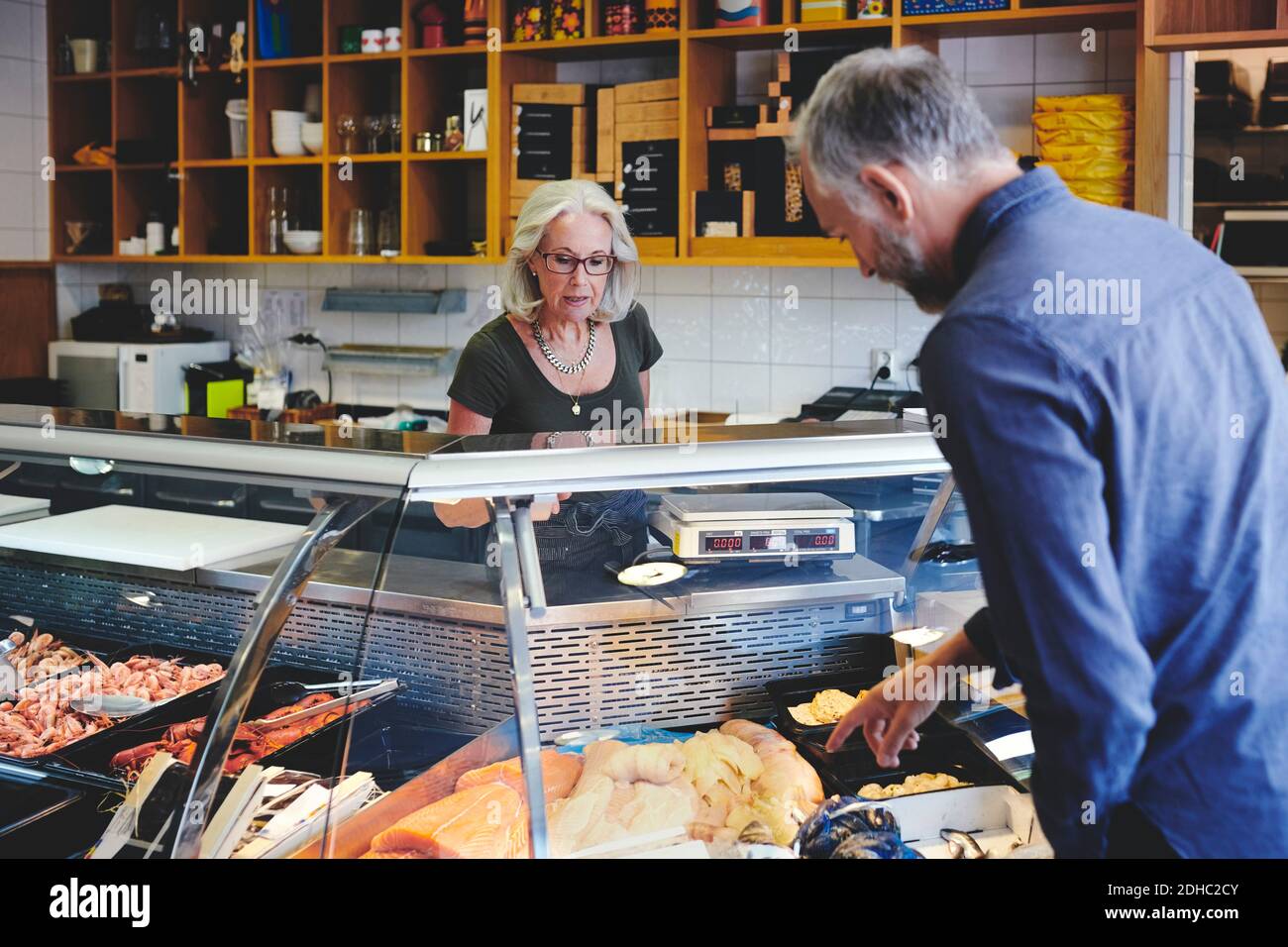 Customer showing seafood at retail display to saleswoman in deli Stock ...