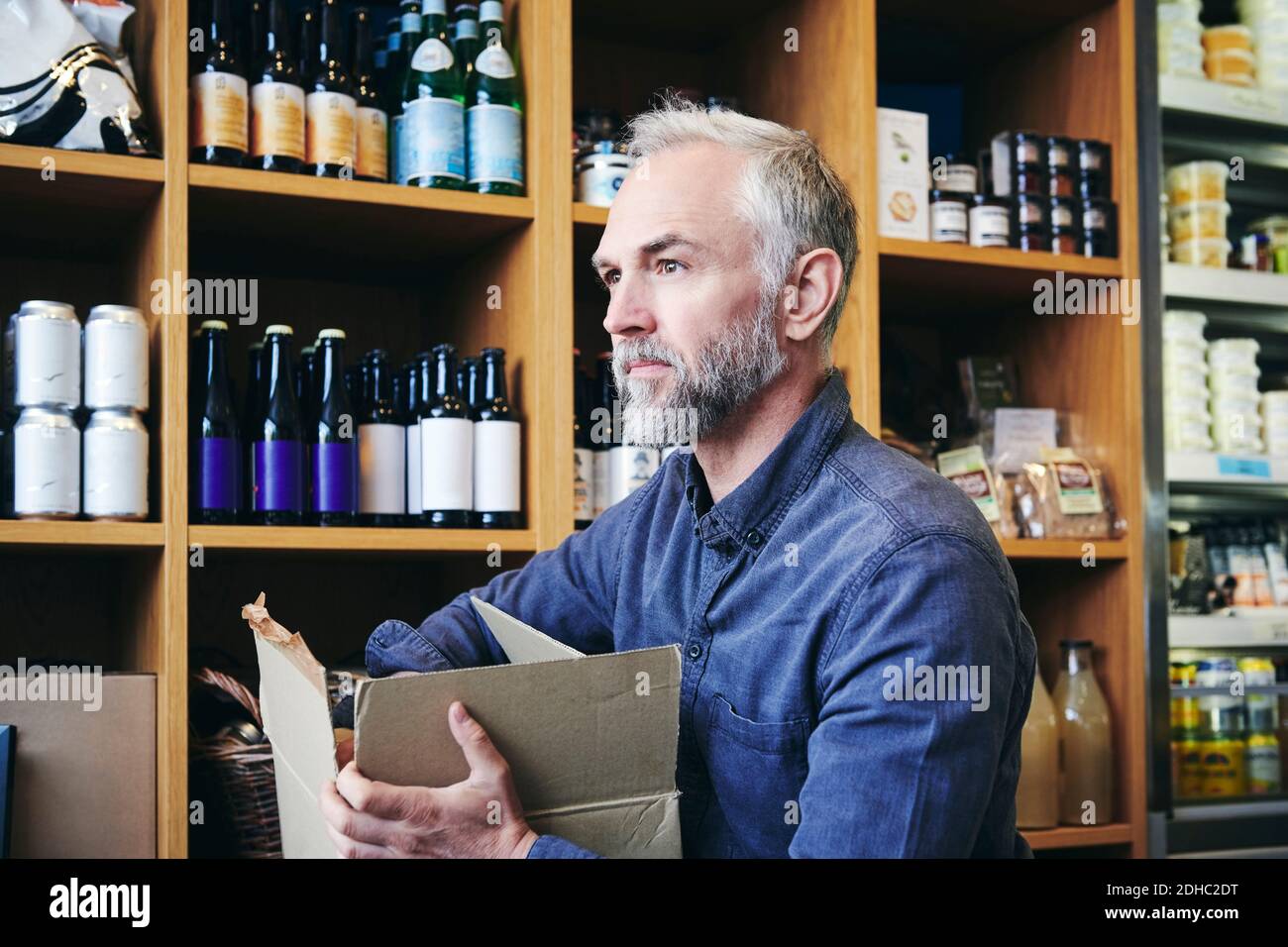 Mature salesman looking away while working in deli Stock Photo - Alamy