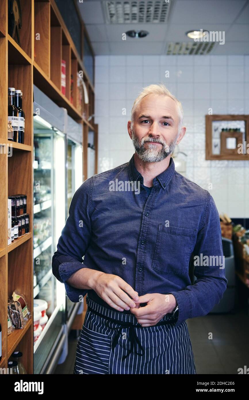 Portrait of mature salesman standing by rack in deli Stock Photo - Alamy