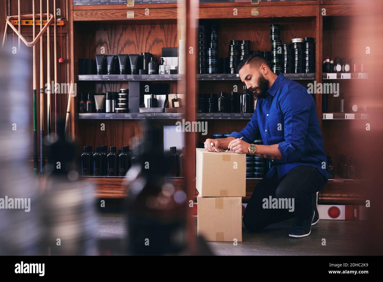 Salesman kneeling while writing on paper by rack in deli Stock Photo ...